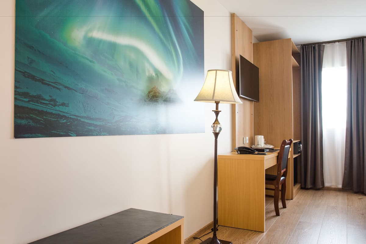 Quarto de hotel com escrivaninha, cadeira, luminária, TV e uma pintura grande da aurora boreal.