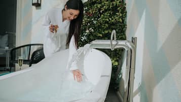 Uma mulher vestindo um roupão branco parada perto de uma banheira com água corrente.