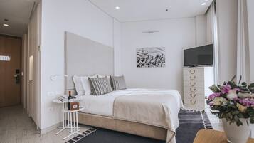 Quarto moderno com cama, televisão, uma mesinha com uma garrafa e um vaso com flores.