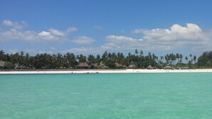 Uma praia com águas turquesa cristalinas, palmeiras e cabanas com telhado de palha.