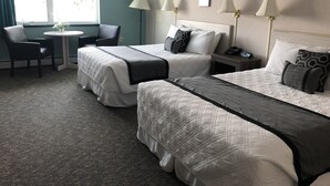 Quarto de hotel com duas camas, uma escrivaninha, cadeiras e luminárias.