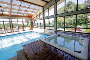 Piscina com hidromassagem, deck de madeira e grandes janelas com vista para a paisagem ao redor.