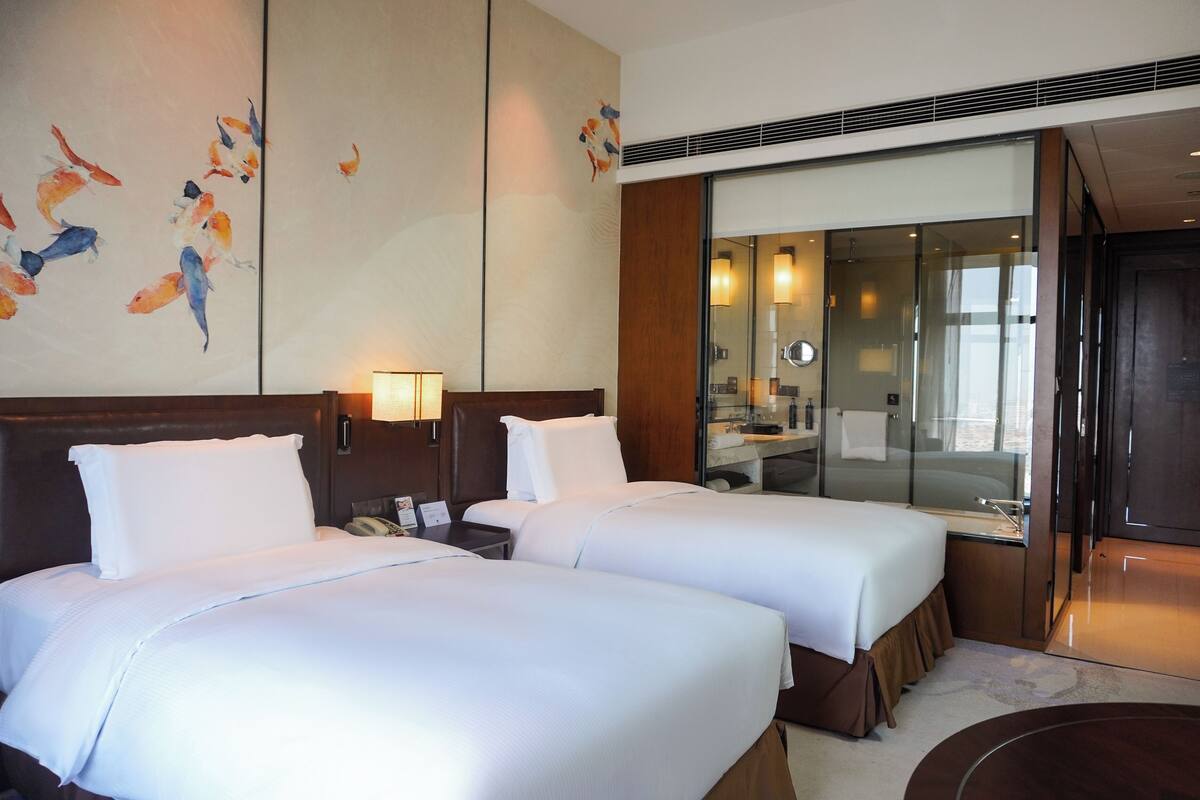 Quarto de hotel com duas camas, um espelho grande e uma parede com pintura de carpas koi.