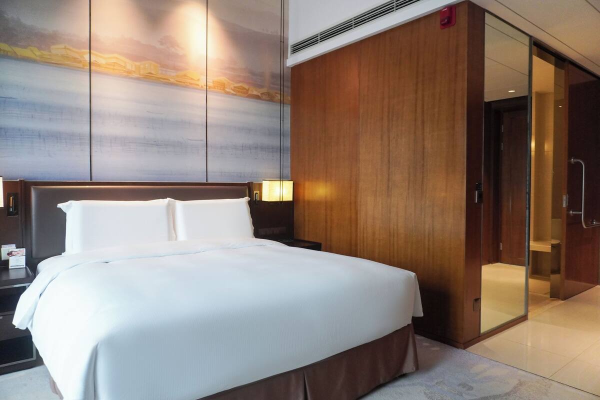 Quarto de hotel com uma cama grande, um guarda-roupa de madeira, uma mesa de cabeceira e uma luminária na parede.