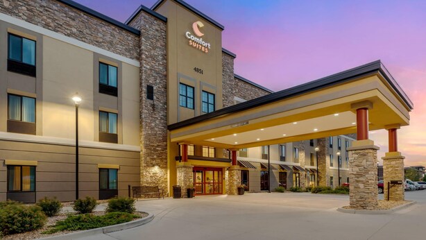 Um hotel com fachada de pedra, entrada coberta e uma placa com a inscrição 'Comfort Suites'.