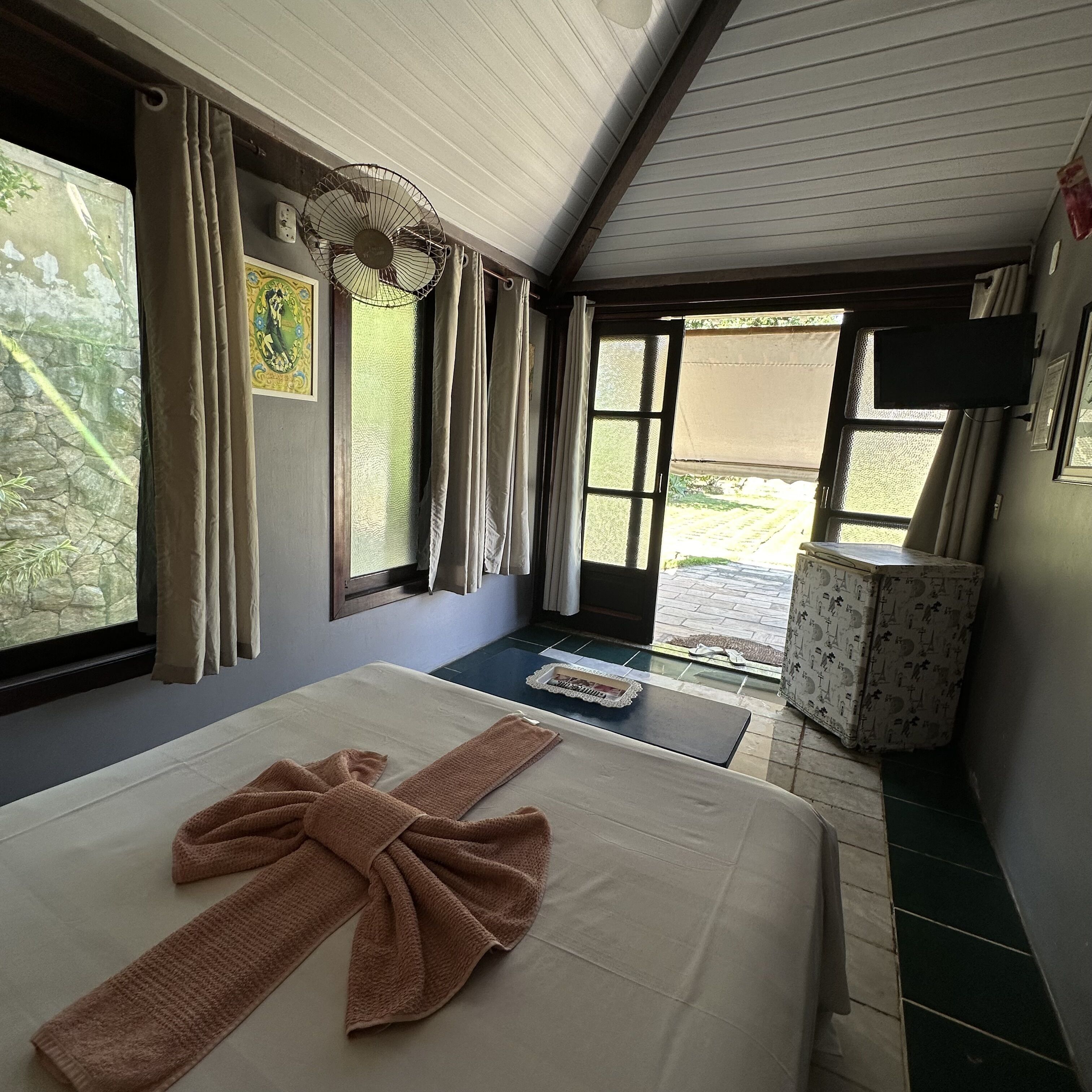 Quarto com cama, ventoinha, televisão e vista para o exterior.