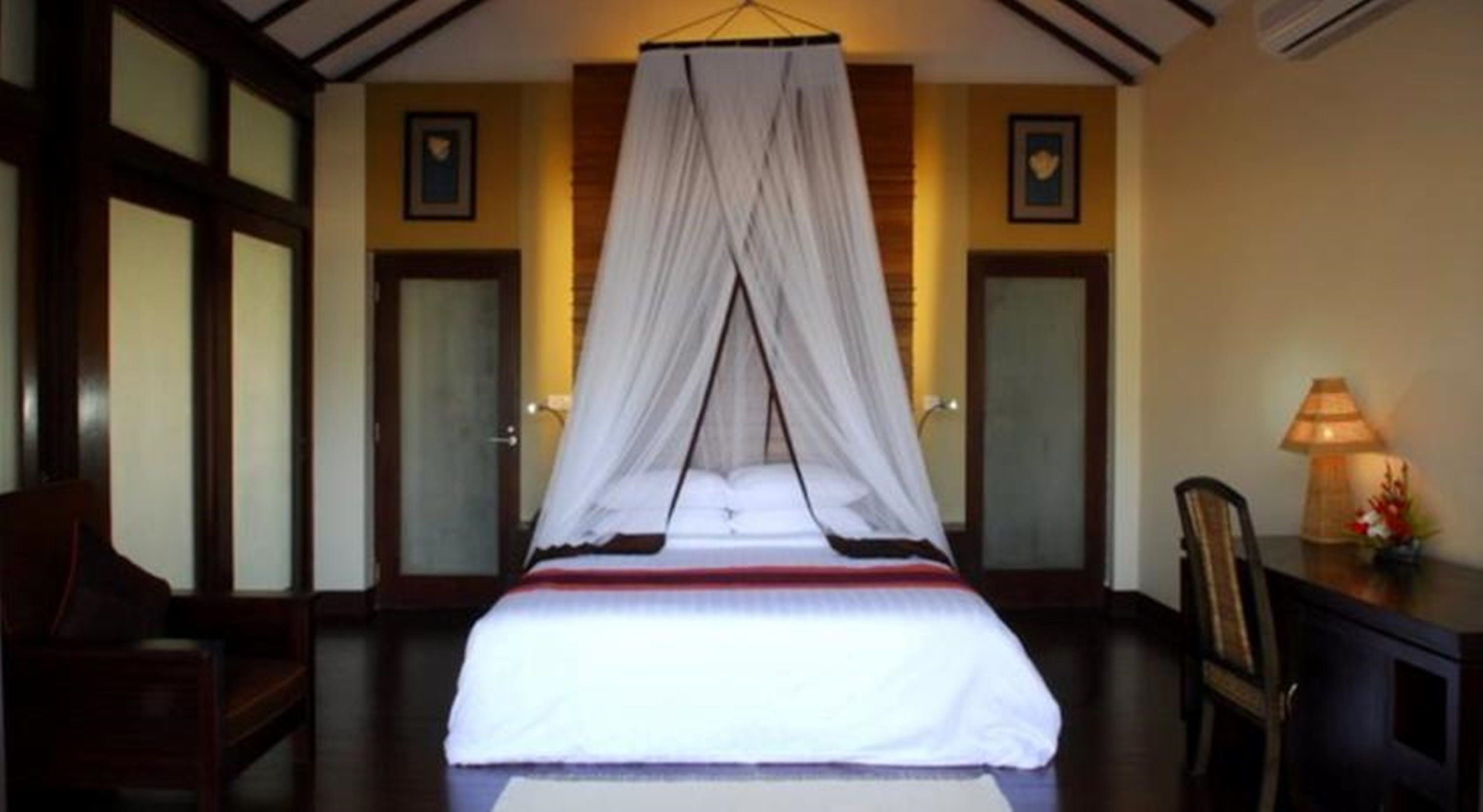 Quarto com cama de dossel, mobiliário de madeira e abajur em uma mesinha de cabeceira.