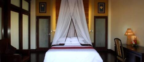 Quarto com cama de dossel, mobiliário de madeira e abajur em uma mesinha de cabeceira.