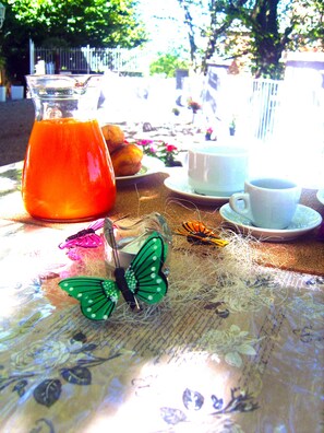 Uma mesa com um copo de suco de laranja, doces, uma chávena de chá e uma decoração de borboleta.
