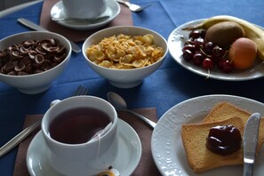 Uma mesa de café da manhã com cereais, frutas, torradas com geleia e uma xícara de chá.