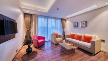 Uma sala de estar moderna com televisão de tela plana, uma poltrona vermelha, um sofá bege com almofadas laranja e uma mesa de centro de madeira.