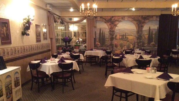 Um restaurante com várias mesas e cadeiras, um candelabro e um mural na parede.