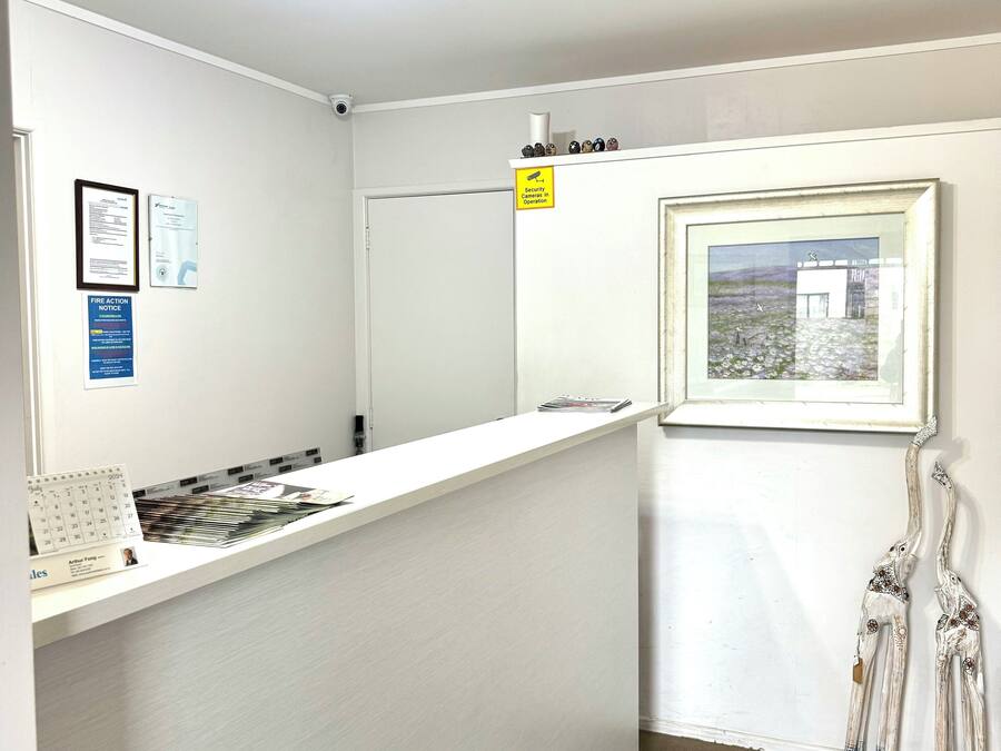 Uma área de recepção com um balcão branco, quadro emoldurado e uma pequena janela.