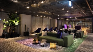 Uma área de estar moderna com um sofá verde, poltronas roxas e um espaço de bar com um computador.