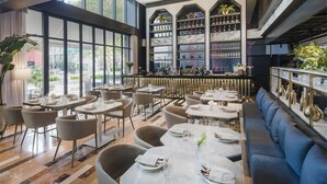 Um restaurante moderno com área de bar, janelas amplas e diversas opções de assentos.