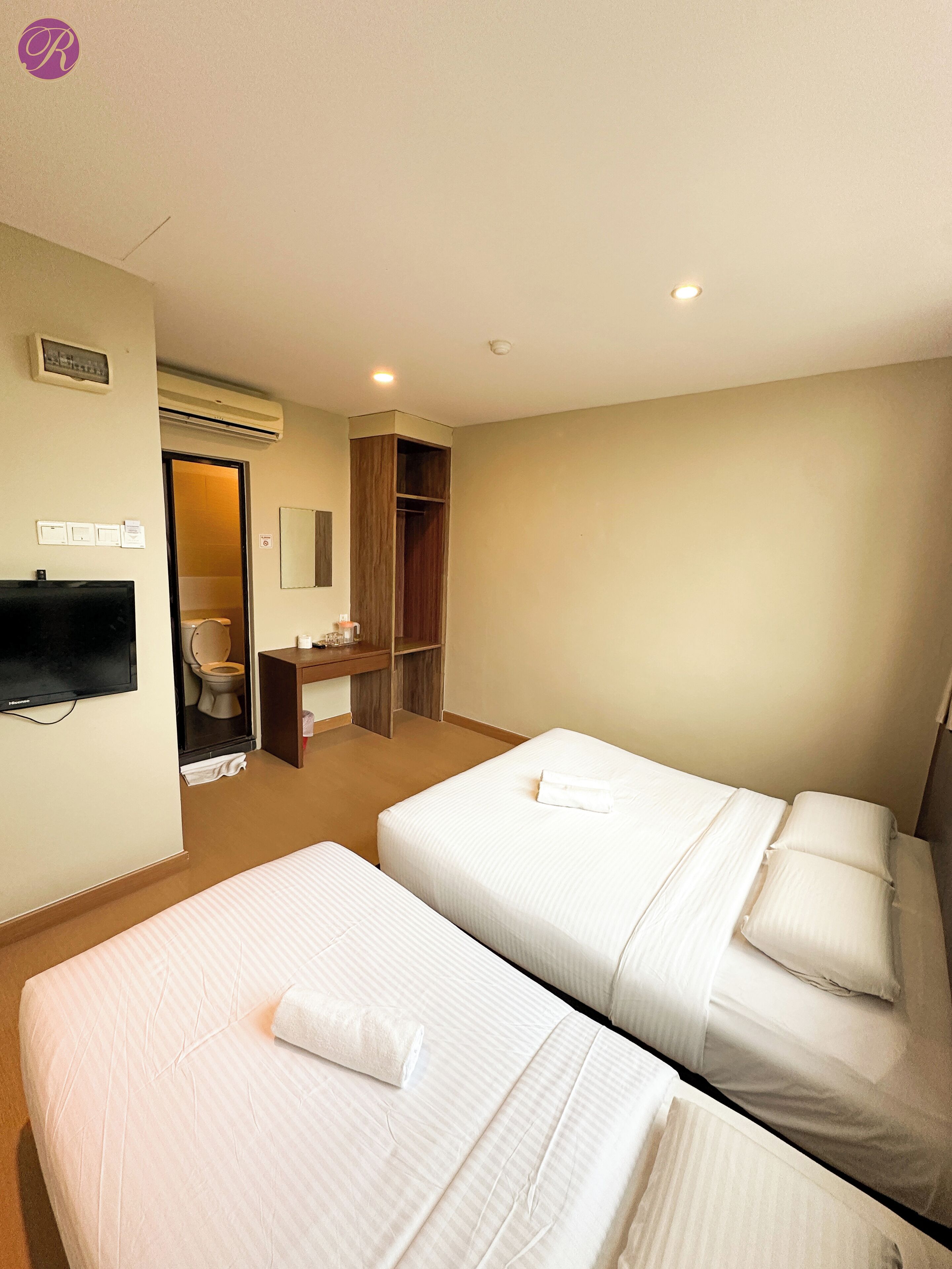 Quarto de hotel com duas camas, televisão, secretária e casa de banho.