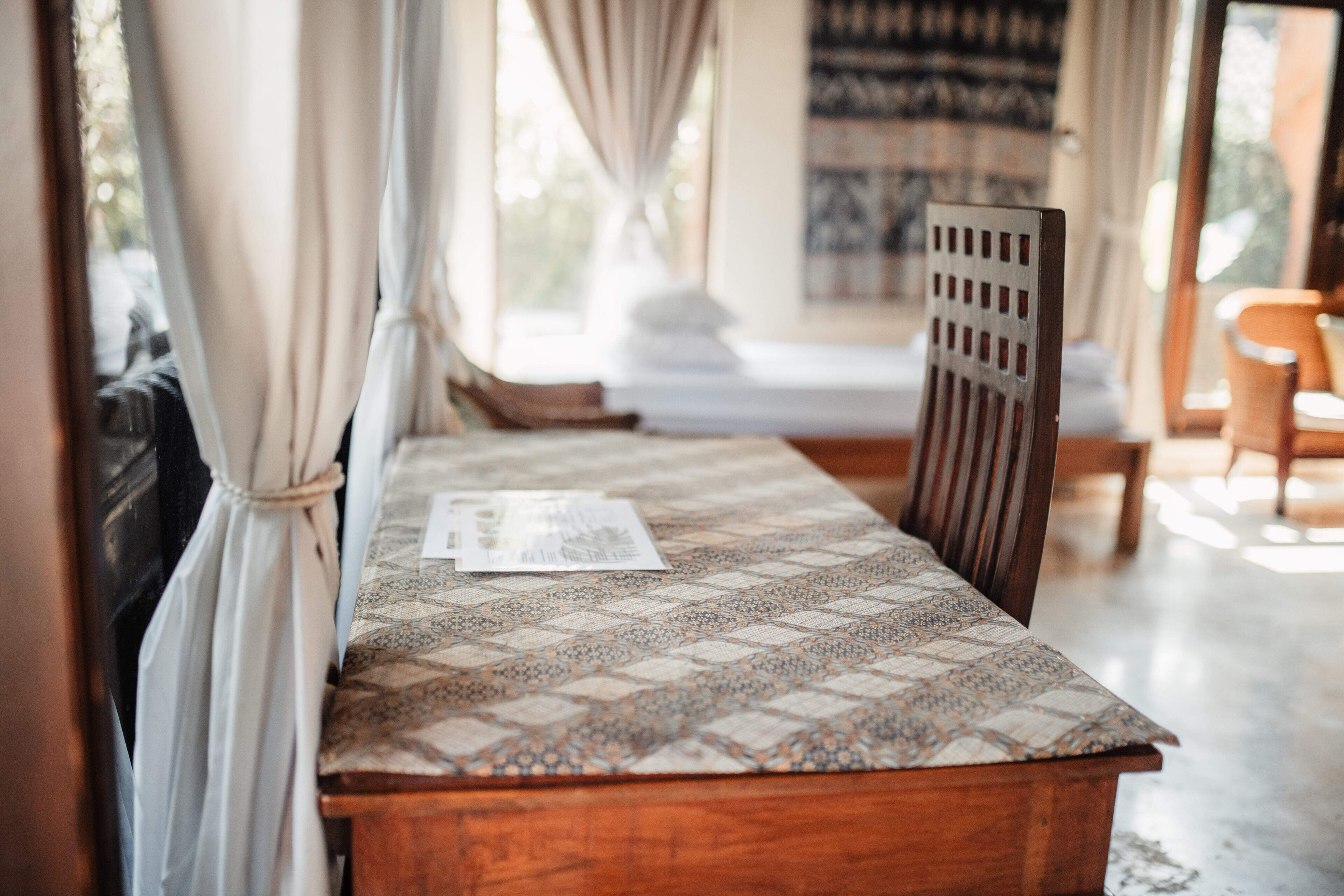 Um banco de madeira com almofada estampada, uma cadeira e uma janela com cortinas.