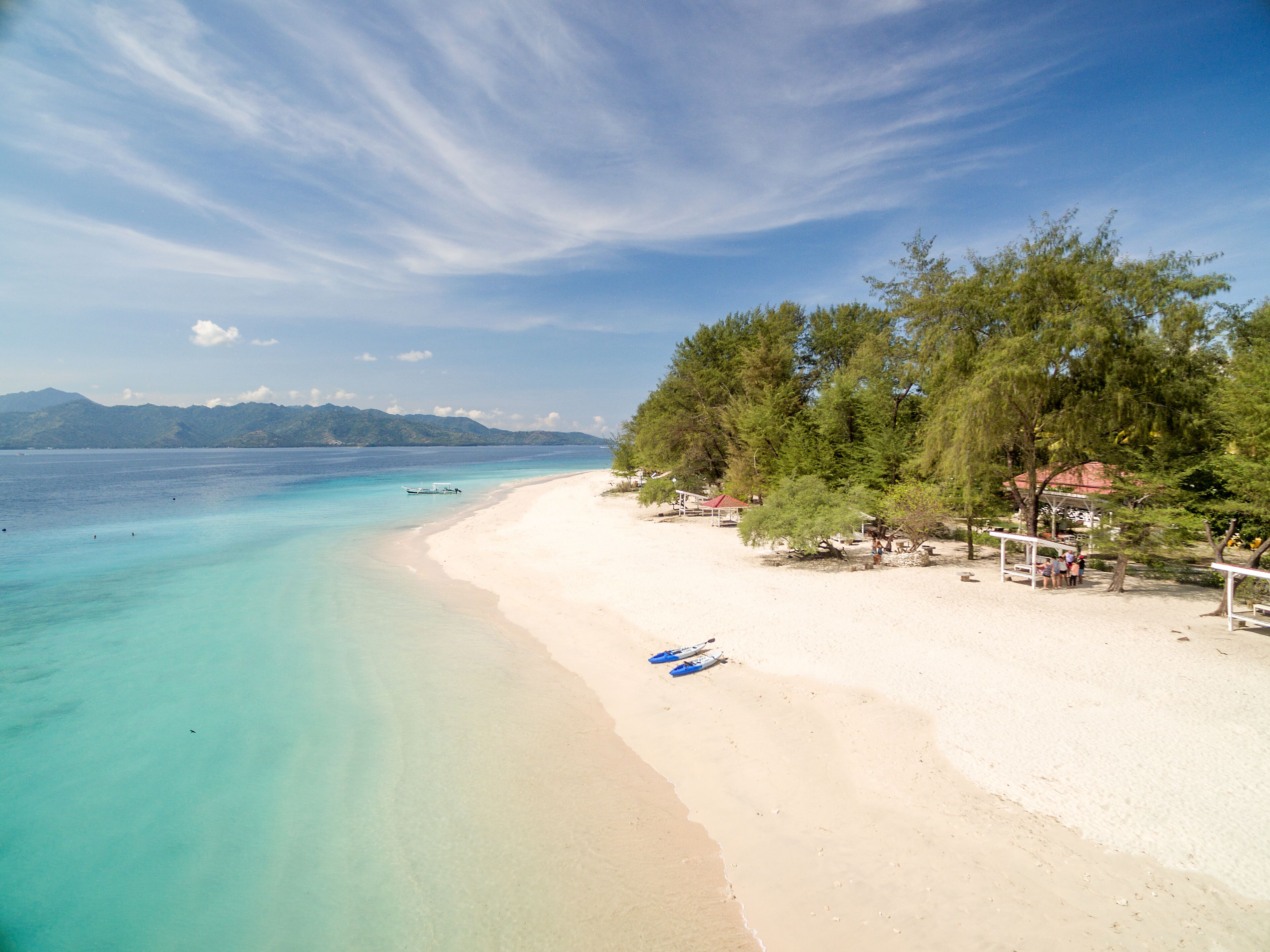 Uma praia com águas turquesa cristalinas, uma orla arenosa e uma fileira de árvores.