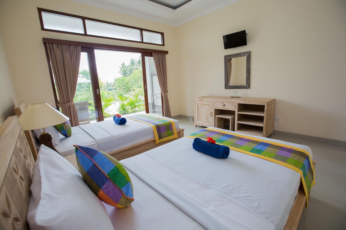 Quarto de hotel com duas camas, um armário de madeira, uma televisão e uma janela com cortinas.