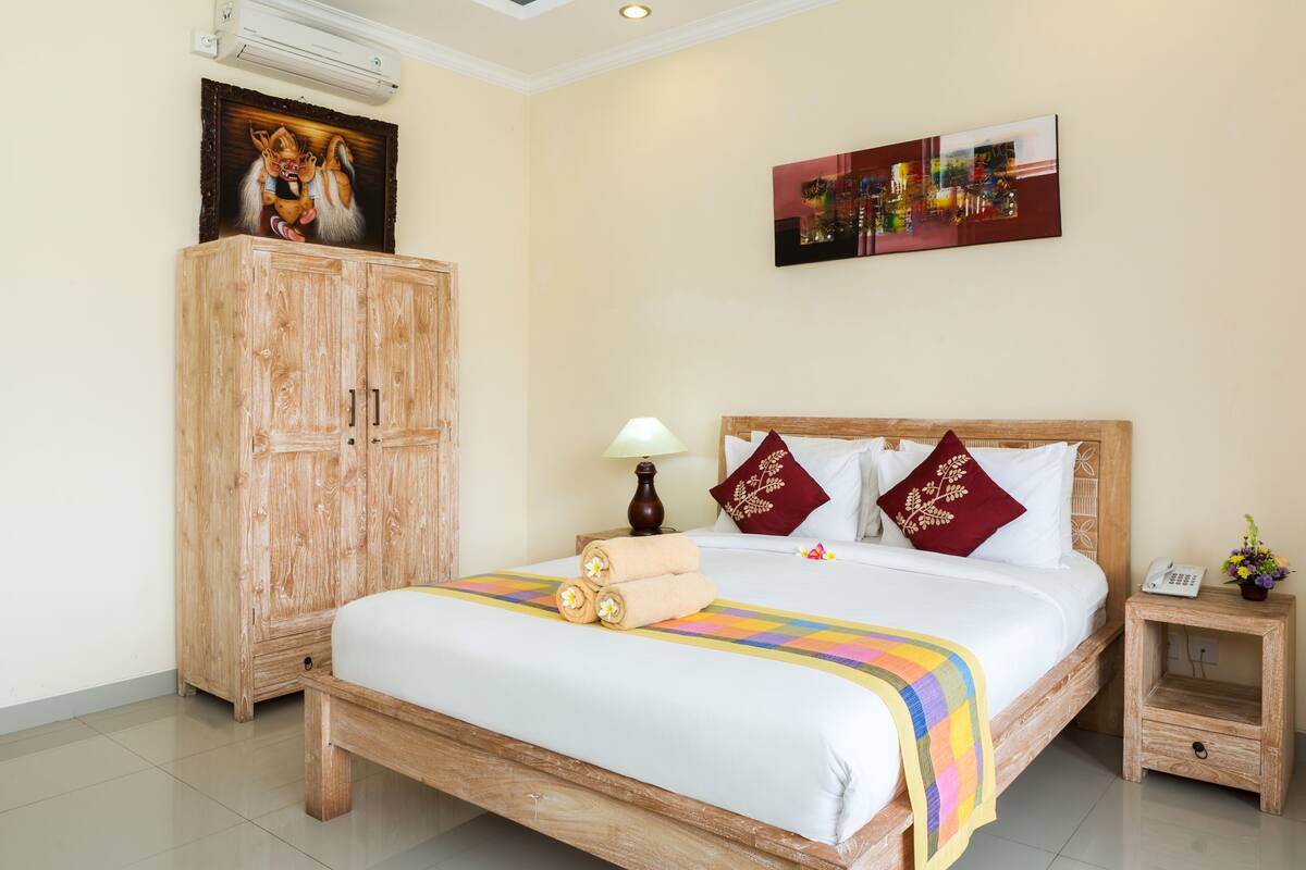 Quarto bem arrumado com cama de madeira, guarda-roupa de madeira, mesa de cabeceira com abajur e um quadro pendurado na parede.