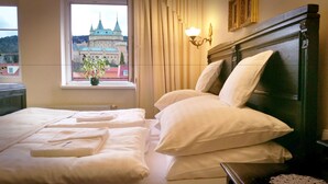 Quarto de hotel com duas camas, vista de um castelo pela janela e luminária fixada na parede.