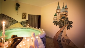 Uma área de spa com um mural em mosaico, uma banheira de hidromassagem rodeada por velas e uma planta decorativa.