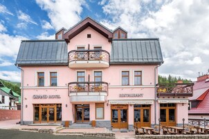 Um edifício rosa com uma placa para GRAND HOTEL e RESTAURANTE.