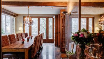 Uma sala de jantar com uma longa mesa de madeira e cadeiras, janelas amplas e um candelabro.