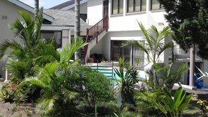 Uma casa de dois andares com escadaria que leva ao andar superior, rodeada por vegetação tropical.