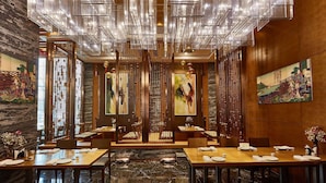 Um restaurante com várias mesas, uma escadaria central e obras de arte nas paredes.