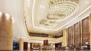 Um hall espaçoso com um lustre imponente, um balcão de recepção e um painel decorativo.