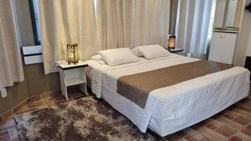 Quarto de hotel com cama, mesas de cabeceira, luminária, geladeira e tapete.