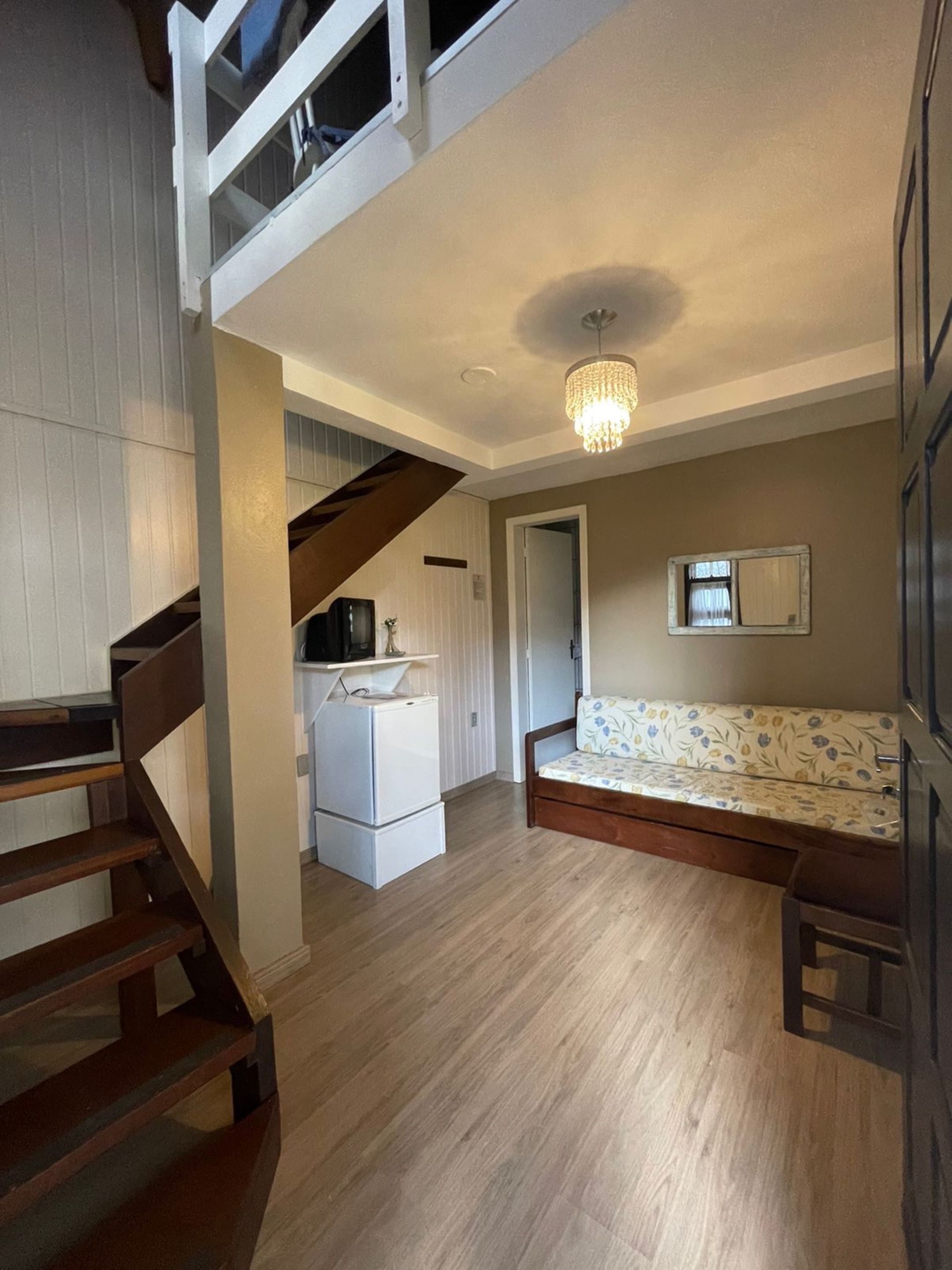 Um interior moderno com escada de madeira, área de jantar com geladeira branca e sala de estar com sofá estampado.
