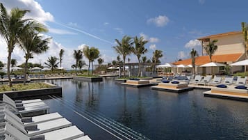 Área de piscina de resort com espreguiçadeiras, palmeiras e céu claro.