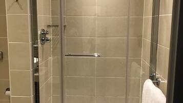 Divisória de chuveiro envidraçada com banheira branca, porta-toalhas e suporte para papel higiênico.