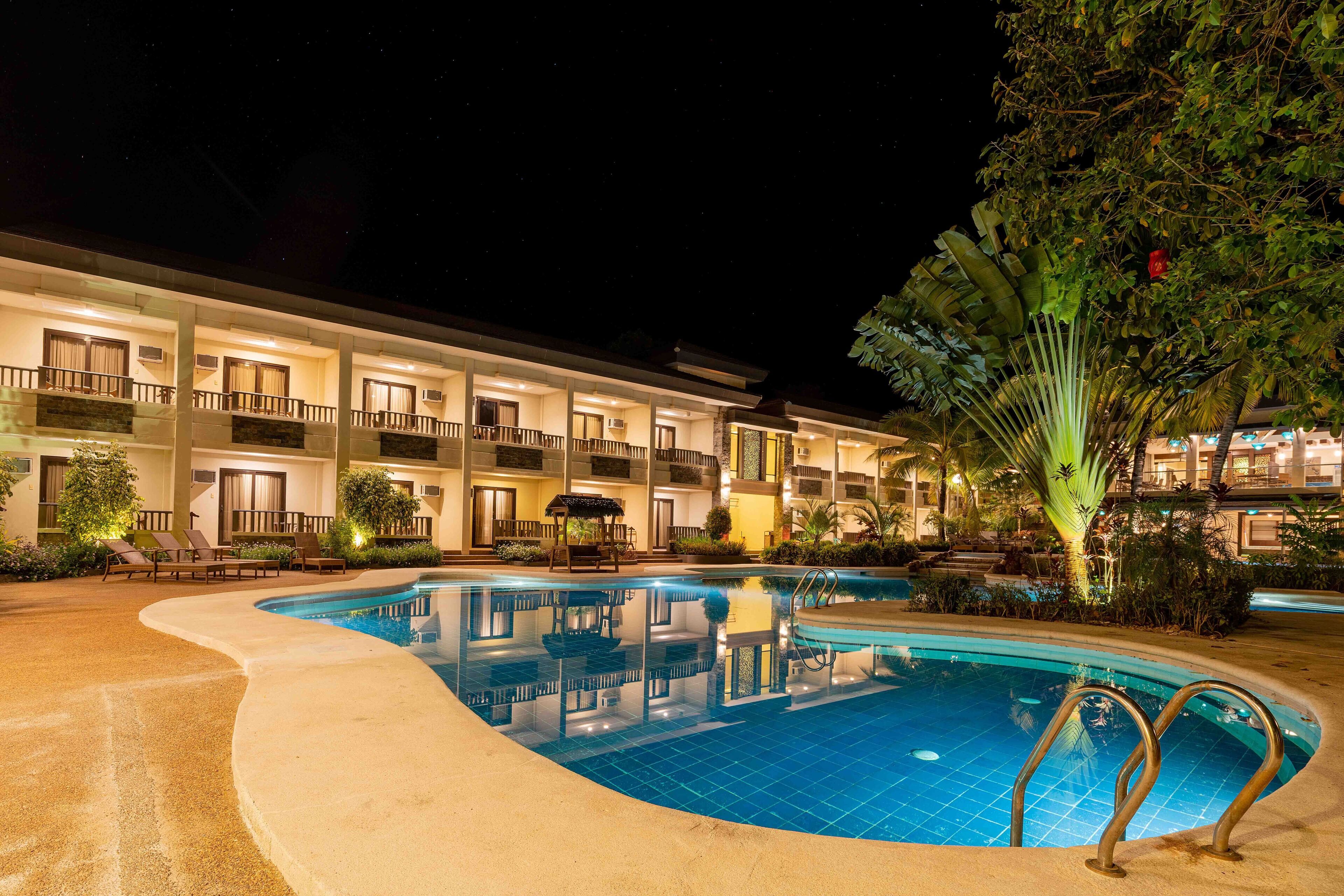 Um hotel com piscina, área de estar externa e fachada bem iluminada à noite.