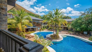 Resort com uma piscina grande, palmeiras e montanhas ao fundo.