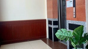 Um saguão de hotel com piso de mármore, uma planta em vaso, um elevador e um painel com uma placa.