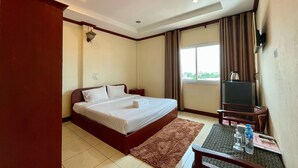 Quarto de hotel com uma cama, uma escrivaninha com cadeira, televisão e janela com cortinas.