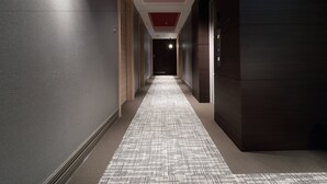 Um corredor moderno de hotel com carpete estampado, paredes de madeira escura e teto vermelho.