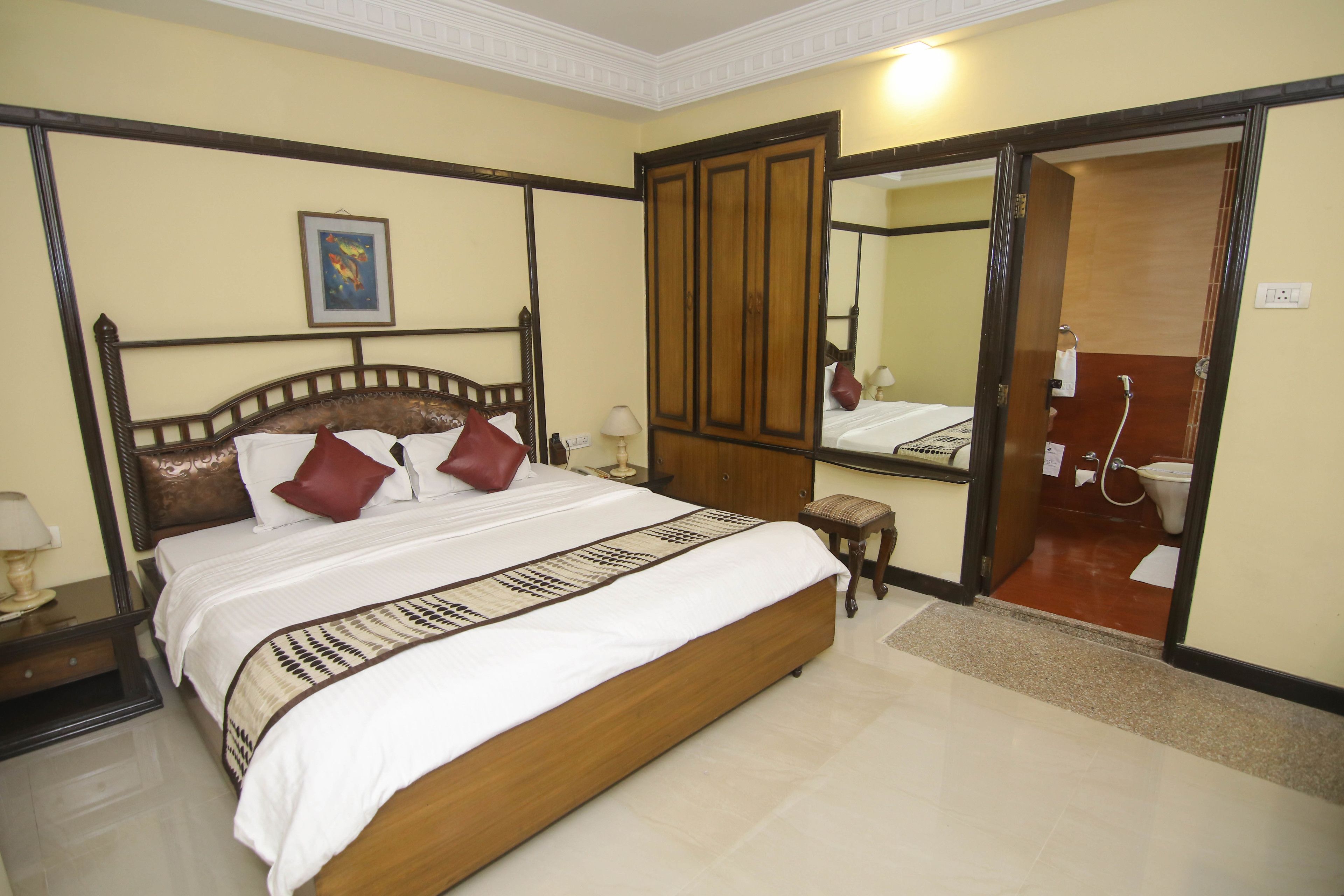 Quarto de hotel bem iluminado com uma cama grande, cabeceira de madeira e um espelho refletindo o banheiro.