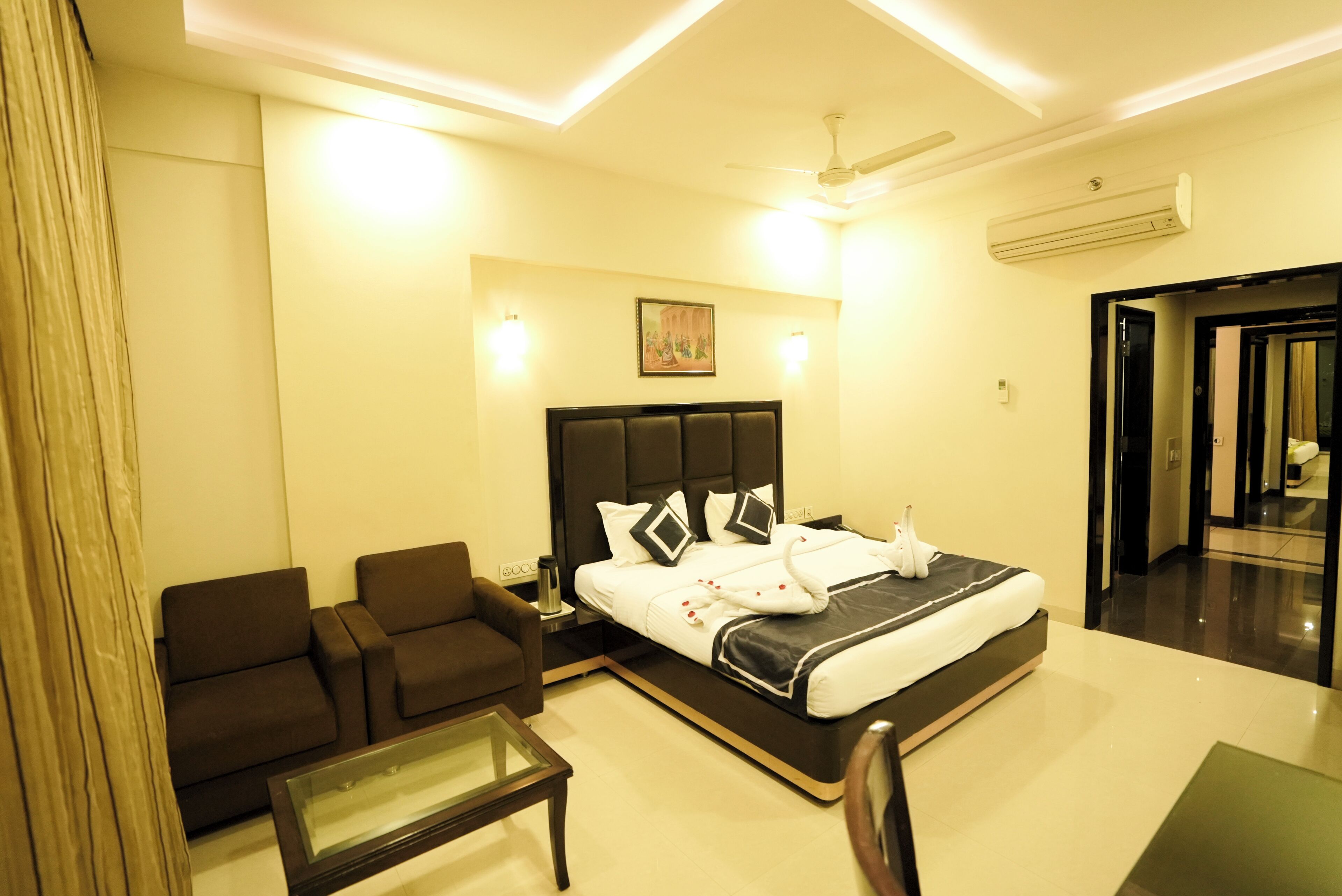 Quarto de hotel com cama, duas poltronas, uma mesinha e um ventilador de teto.