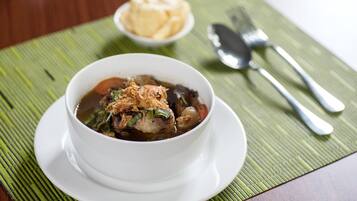 Uma tigela de sopa com carne e legumes, acompanhada de uma pequena tigela de arroz e um garfo sobre um descanso de mesa verde.