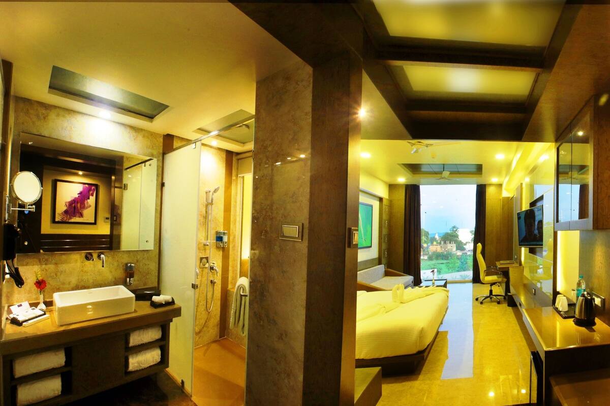 Quarto de hotel com uma cama grande, banheiro com pia e espelho, e vista para o exterior.