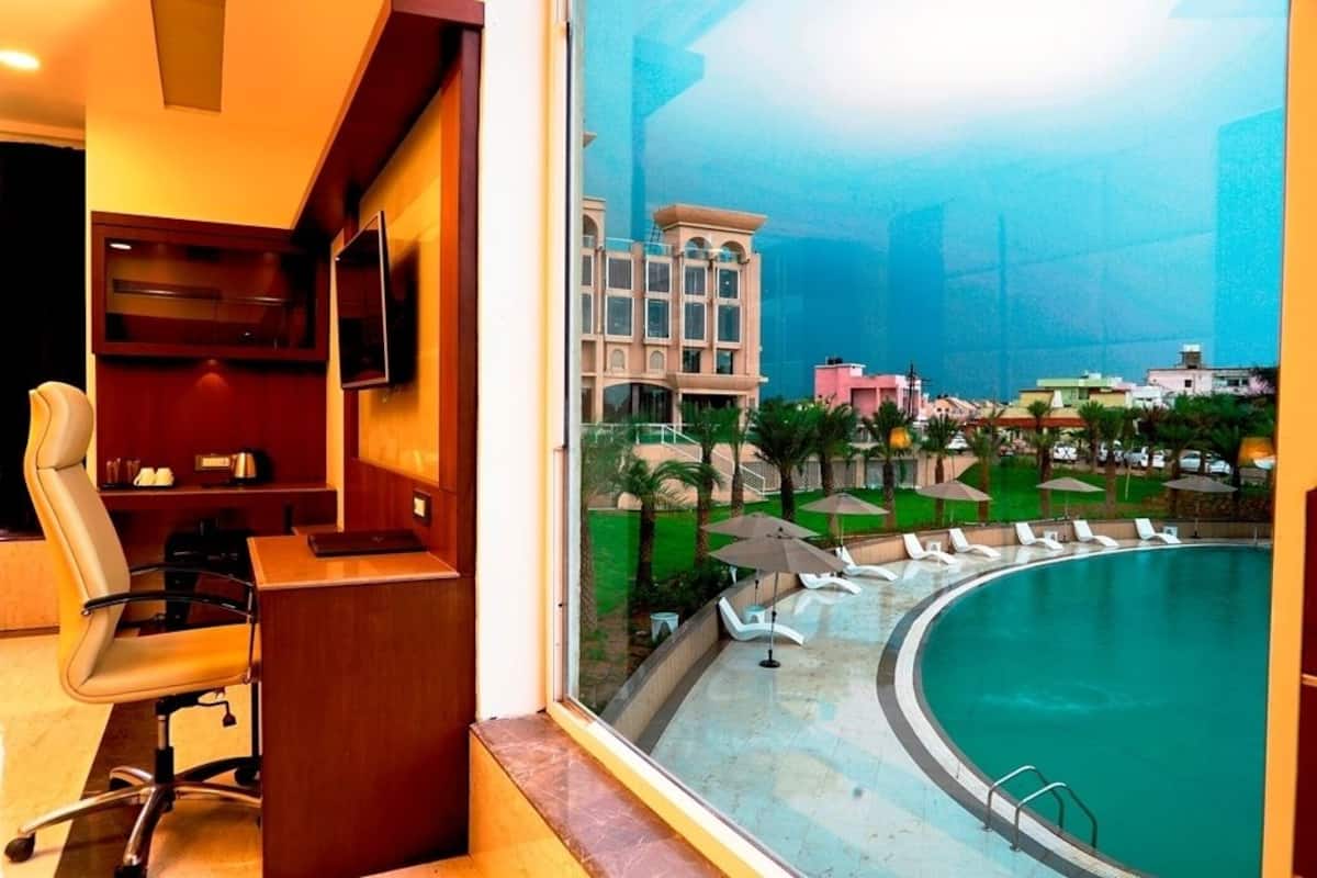 Quarto de hotel com escrivaninha, cadeira e uma grande janela com vista para uma piscina e área de estar ao ar livre.