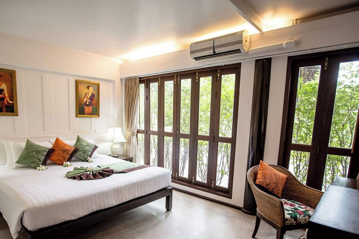 Quarto de hotel com uma cama, duas mesas de cabeceira, uma cadeira e janelas amplas.