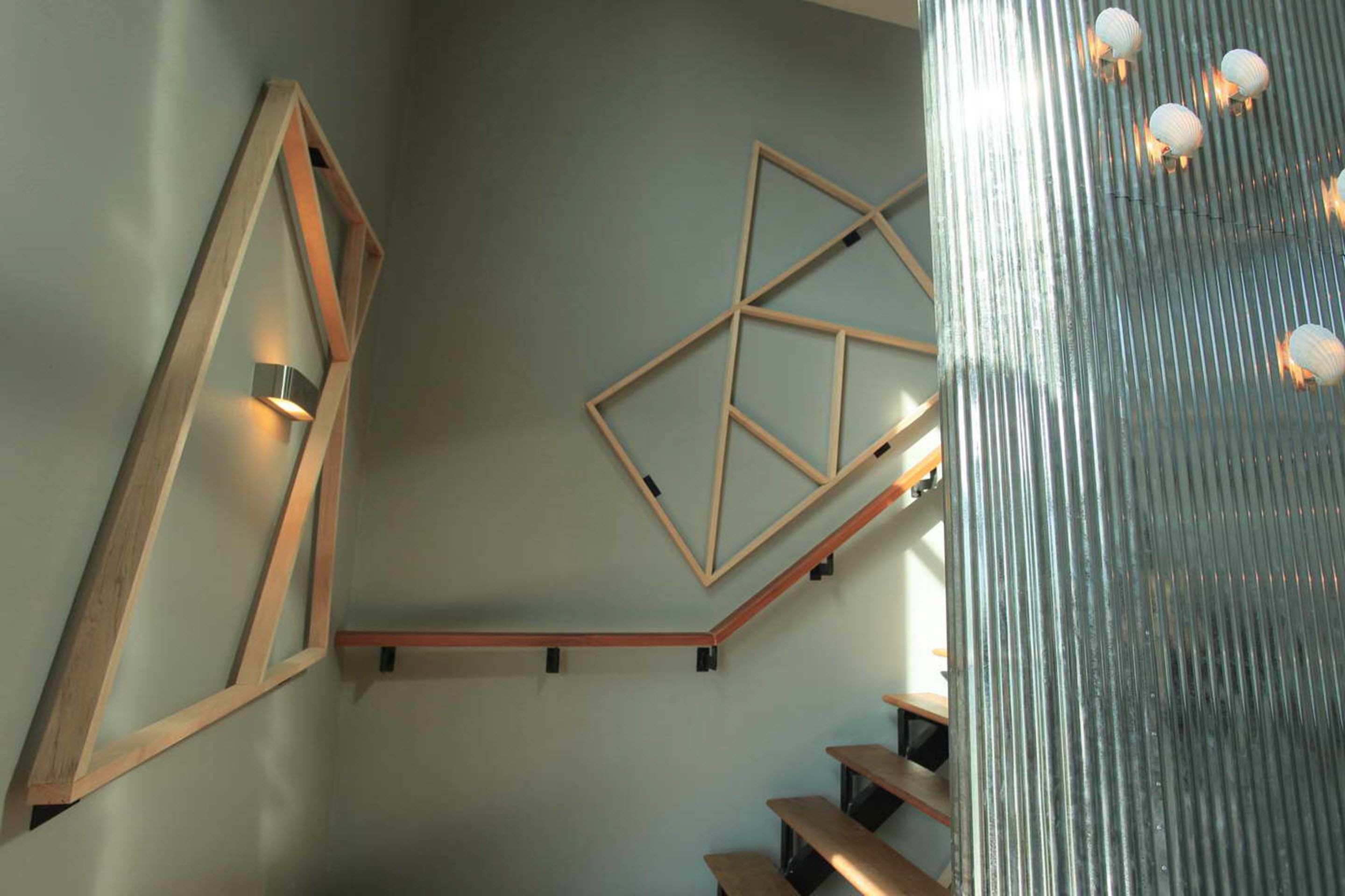 Interior moderno com arte de parede geométrica, uma escada de madeira e um corrimão de metal.
