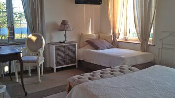 Quarto com duas camas, televisão na parede, uma cadeira, uma mesinha e uma janela com cortinas.