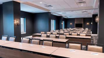 Uma sala de conferência com mesas e cadeiras dispostas em fileiras, uma tela grande e um projetor.