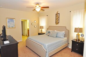 Quarto com cama, mesas de cabeceira, ventilador de teto, escrivaninha e cadeira.